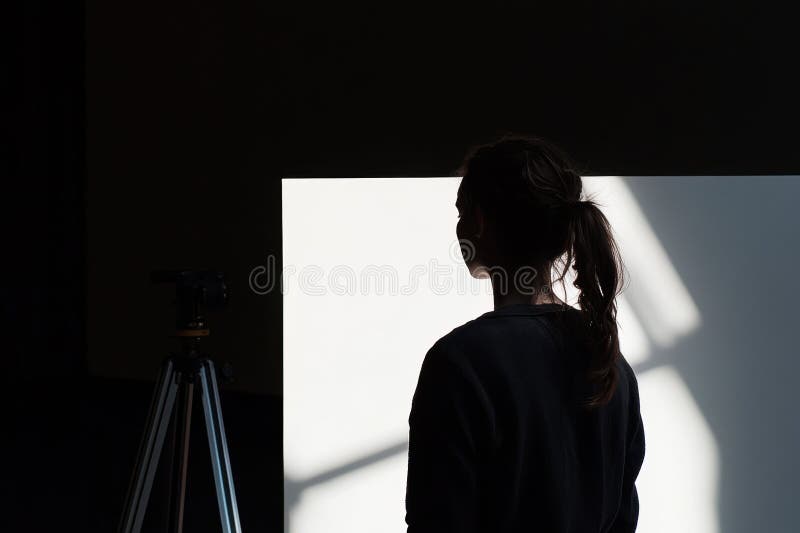 Silhouetted Woman Facing White Wall with Camera Tripod in Foreground ...