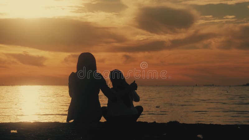 Silhouettes Mother And Daughter Sit On The Beach At Sunset Concept Of