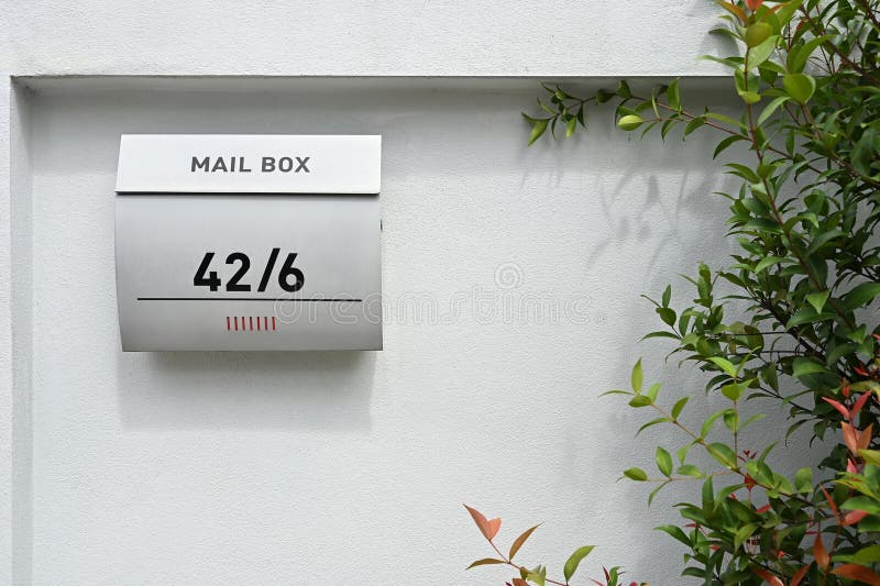 A Silver Mailbox with the Number on a White Wall Near Plants Stock ...