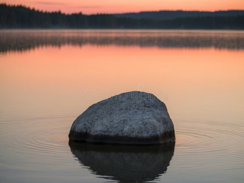 A Single Rock Sits in the Middle of a Calm Lake at Sunset. Stock Photo ...