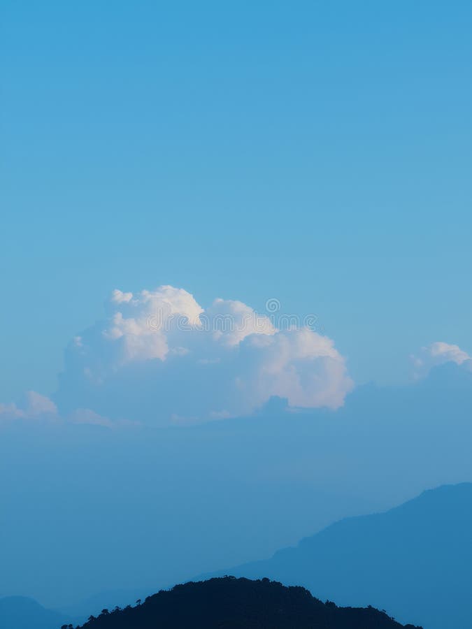 A Single White Cloud Drifts Across a Bright Blue Sky Above a Mountain ...
