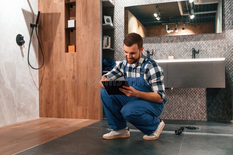 Sitting on the Floor with Notepad in Hands. Plumber in Blue Uniform is ...