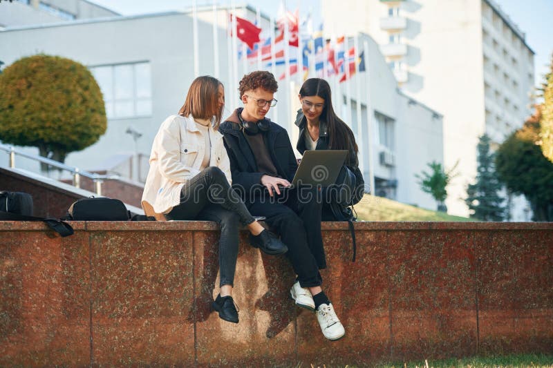 Sitting and Using Laptop. Three Young Students are Outside the ...