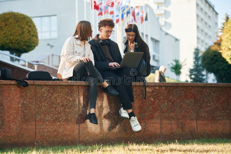 Sitting and Using Laptop. Three Young Students are Outside the ...