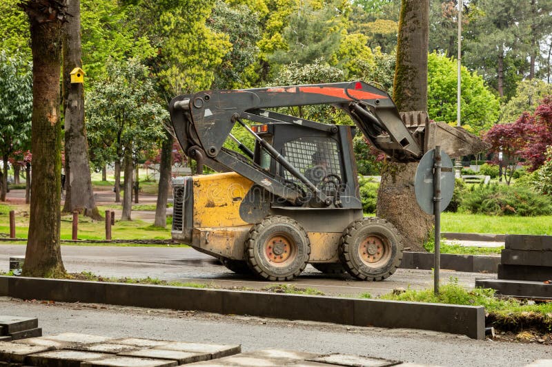 A Skid Steer Loader Operating on a Park Path Surrounded by Trees during ...