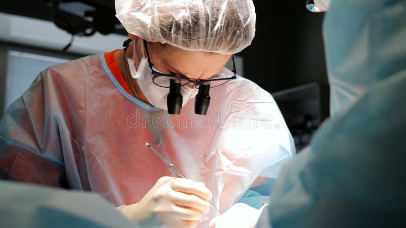 Skilled Surgeon in Surgical Attire, Including a Mask and Loupes ...