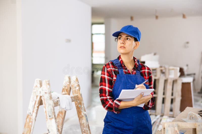 Skilled Woman Builder in Work Clothes Checking Project Documentation ...