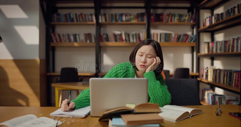 Sleepy Girl Student in a Green Sweater Makes Notes in a Notebook and ...