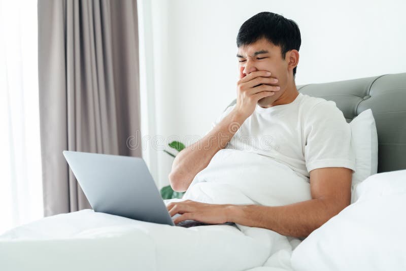 Sleepy Man Yawning on Bed Using Laptop Computer Stock Image - Image of ...