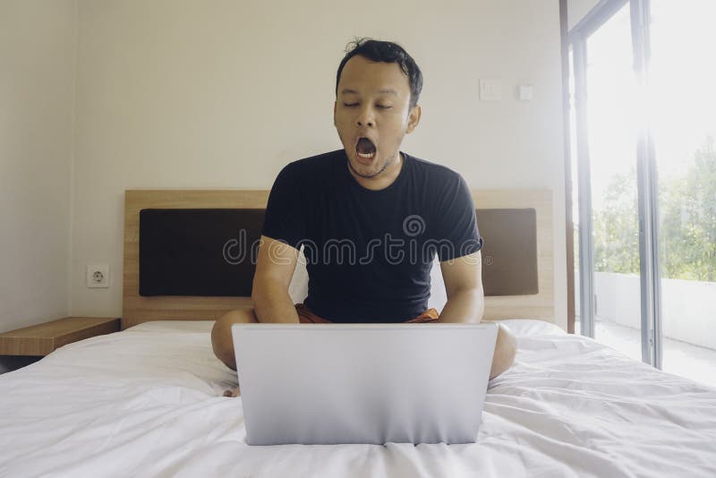 A Sleepy Young Man Yawning while Checking Laptop on the Bed Stock Image ...