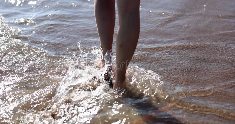 Slender Female Legs And Feet Walking On Waves Of Sea Water On Sandy