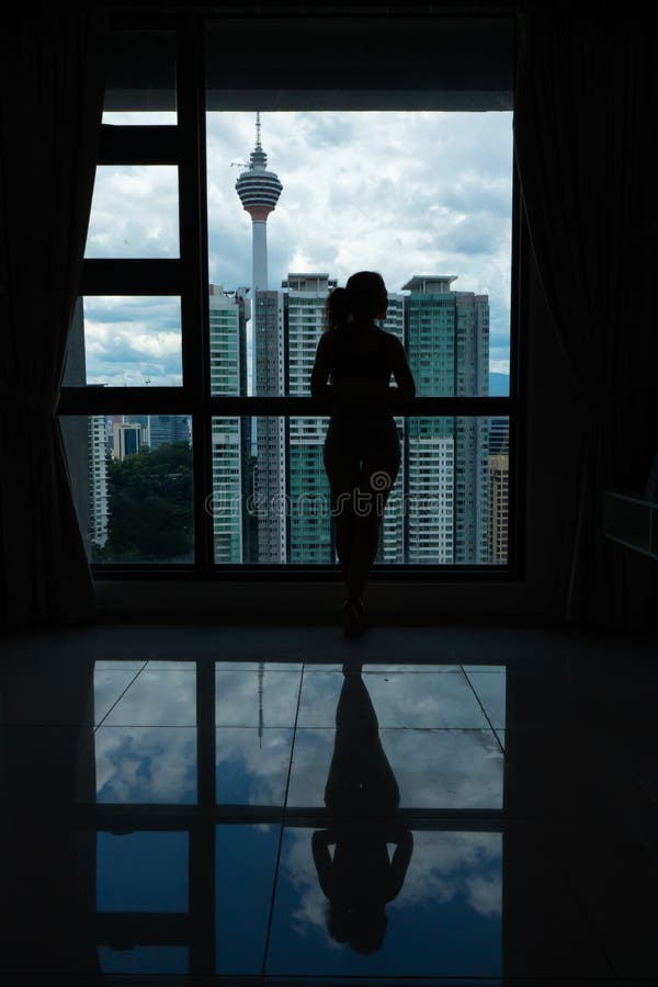A Slender Girl is Looking at the City through a Large Window. High ...