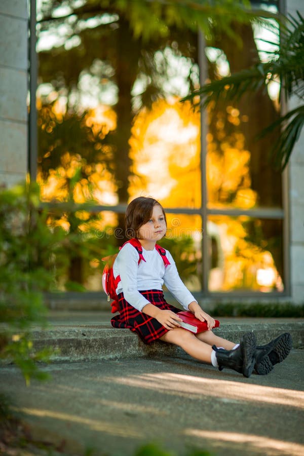 A Small, Beautiful Girl, Sitting on a Bench, in a School Uniform, with ...