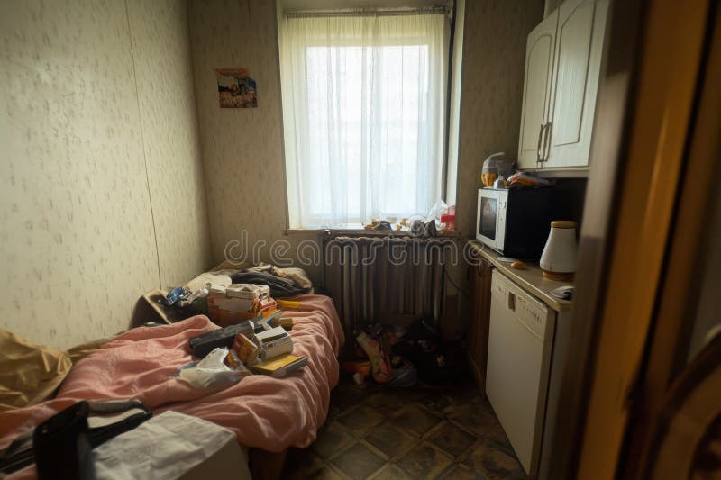 Small Cluttered Room Featuring Bed, Kitchenette, and Window with Soft ...