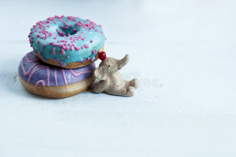 A Small Elephant Figurine Propped Up with Two Different Colored Donuts ...