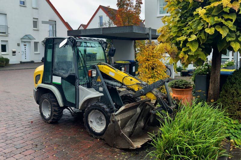 A Small Excavator Standing on the Sidewalk Near a Residential Building ...