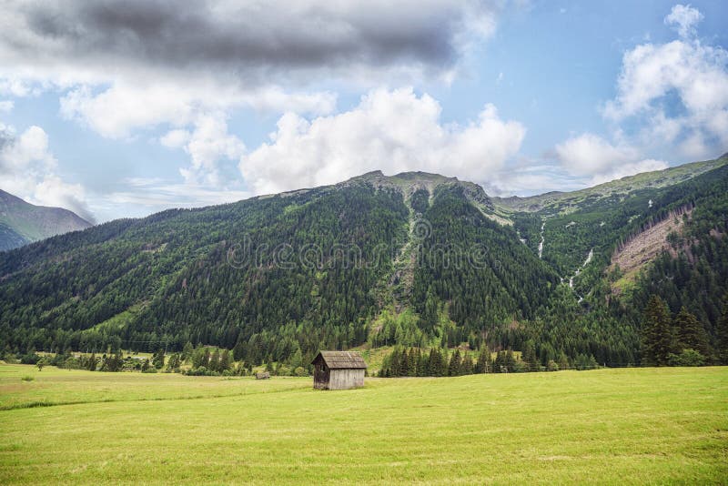 Small Hut on a Green Field Beneath Mountains Stock Photo - Image of ...