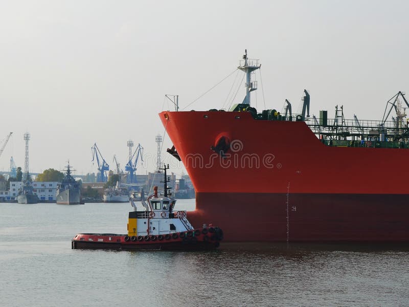 A Small Pilot Ship Leads a Large Red Cargo Ship at the Seaport on a ...