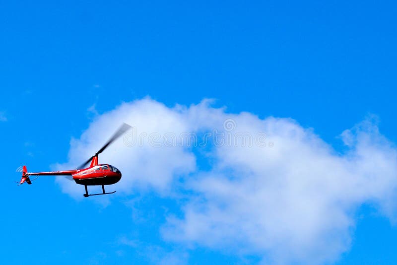 A Small Red Helicopter Flies through the Blue Sky with White Clouds ...