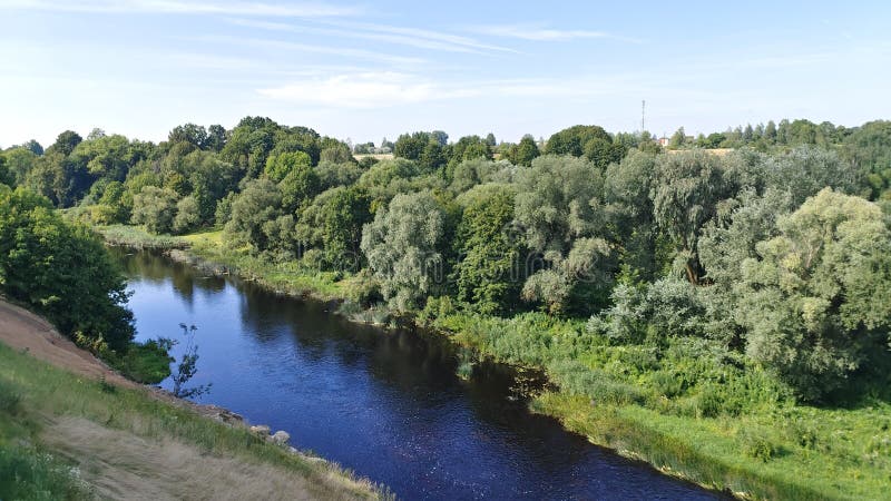 A Small River Flows between High Grassy Banks. Shrubs and Trees Growing ...