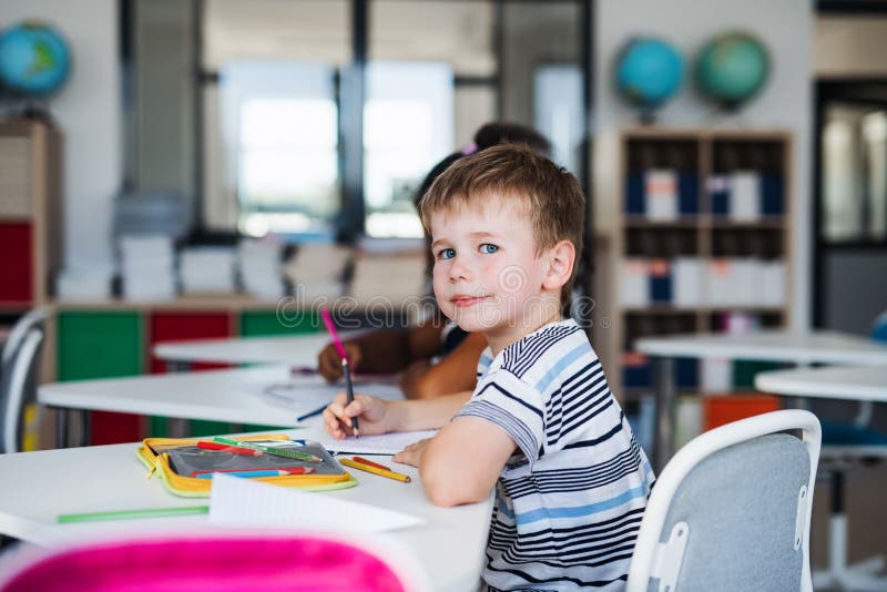 A Small School Boy Sitting at the Desk in Classroom, Writing. Stock ...