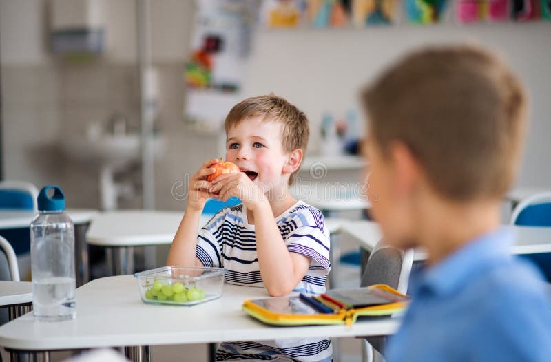Small School Children Sitting at the Desk in Classroom, Eating Fruit ...