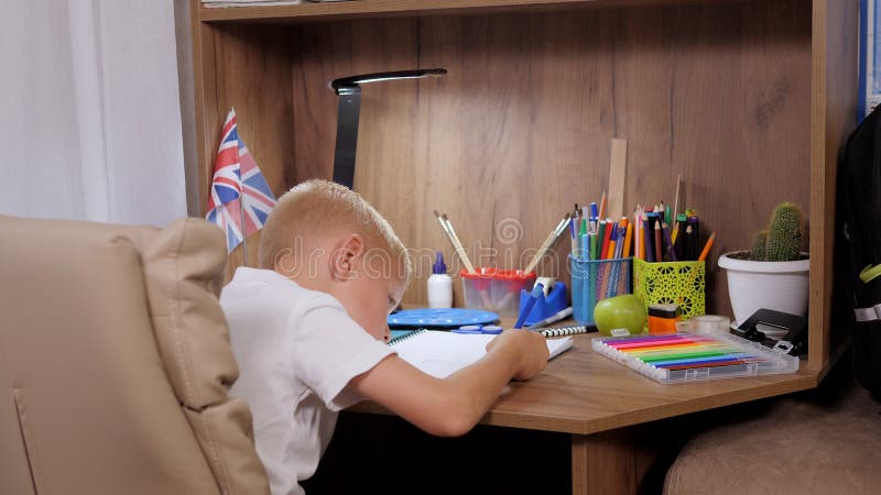 A Schoolboy is Sitting in a Chair at a School Desk and Writing in a ...