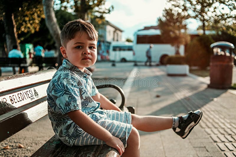Small and Very Cute Boy Sitting on a Bench and Looking at the Camera ...