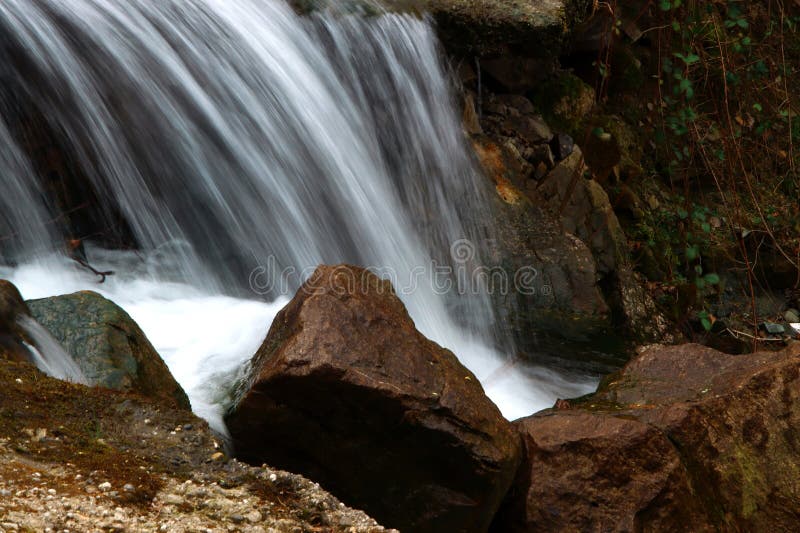 A Small Waterfall Flows Down a Rocky Cliff in a Forested Area Stock ...