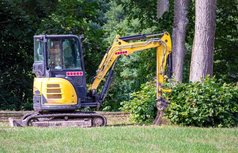 A Small Yellow Tractor with a Bucket and Tracks in the Park Near a Tree ...