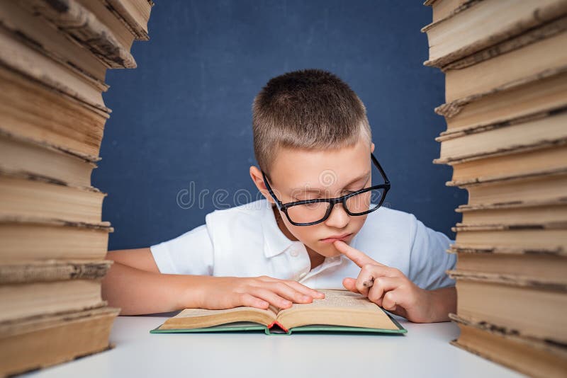 Smart Boy in Glasses Sitting between Two Piles of Books and Read Book ...