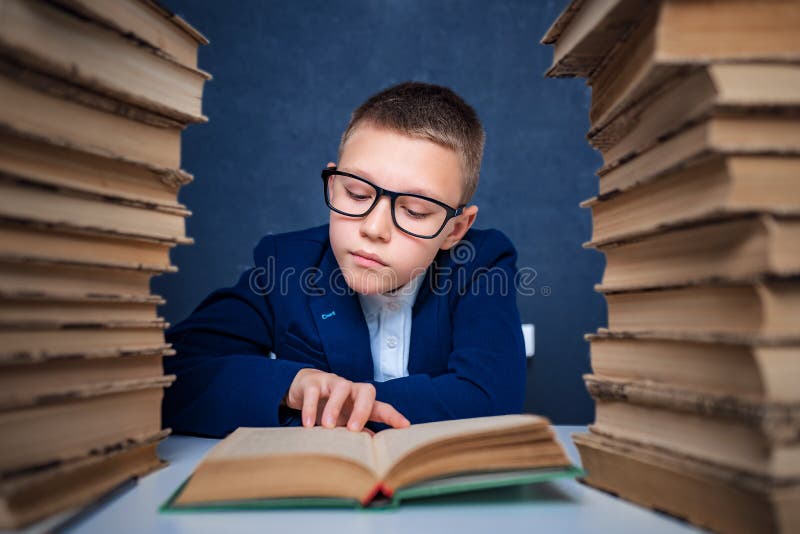 Smart Boy in Glasses Sitting between Two Piles of Books and Read Stock ...
