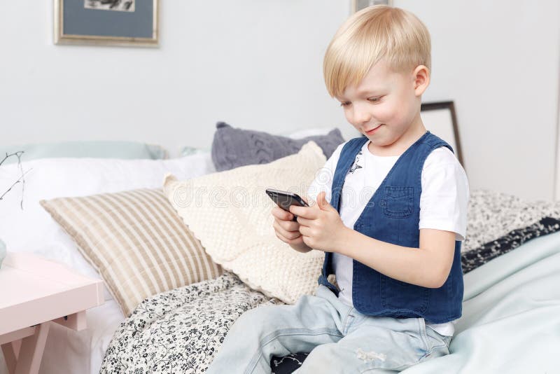 Smart Small Boy with Mobile Phone, Seats on Bed in Bedroom. Technology ...