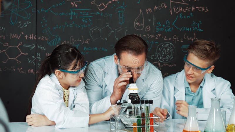 Smart Teacher Looking at Microscope Surrounded by Diverse Student ...