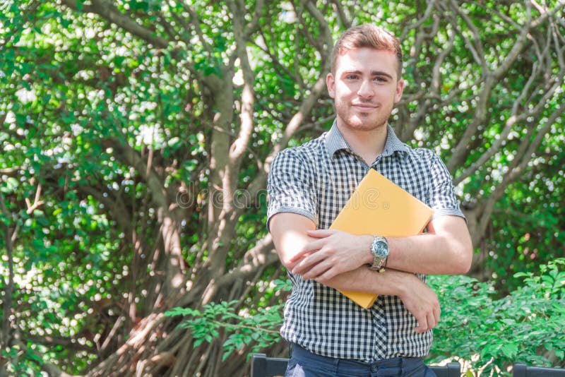 Smart Man Standing Holding a Yellow Book in the Garden Under the Tree ...