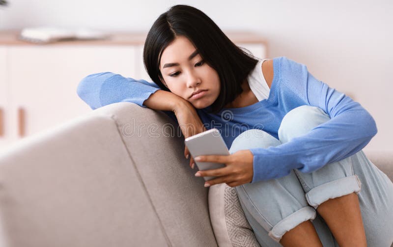 Frustrated Asian Girl Sitting With Smartphone On Couch Emotionally