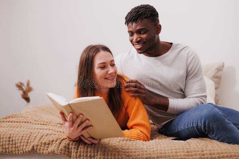 Smiling African American Man Hugging Girlfriend Reading Book at Home ...