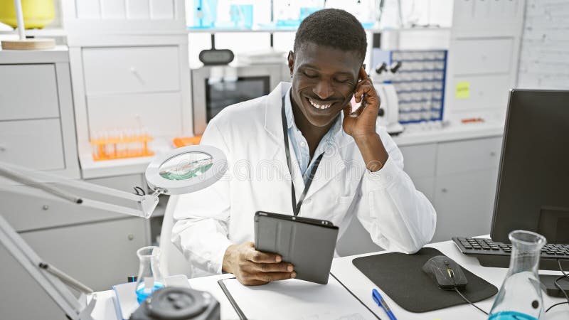 A Smiling African Man in a Lab Coat Using a Tablet in a Modern ...