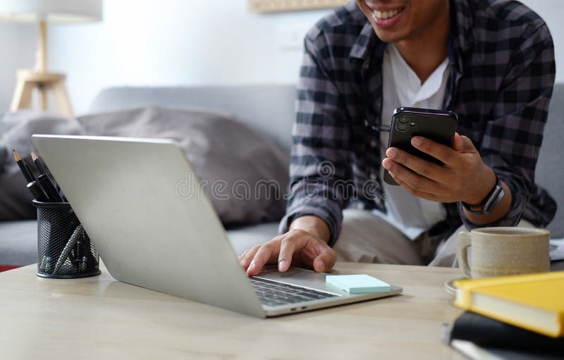 Smiling Asian Man Sitting on Couch Using Laptop Computer and Smart ...
