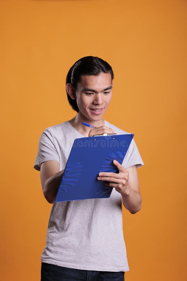 Smiling Asian Man Taking Notes in Blue Clipboard Stock Image - Image of ...