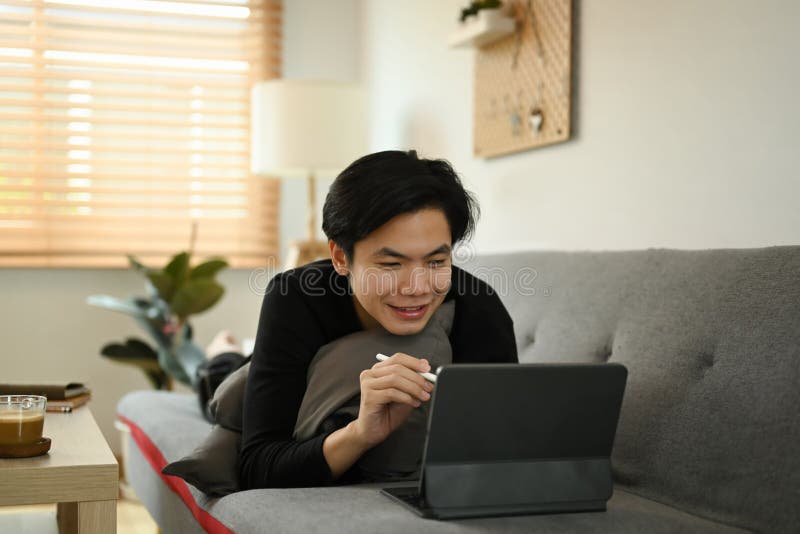Asian Man Using Computer Tablet on Sofa at Home. Stock Image - Image of ...
