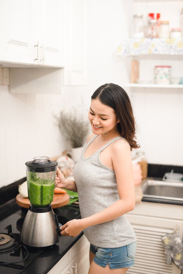 Smiling Asian Woman Making Smoothie With Fresh Vegetables In The Stock