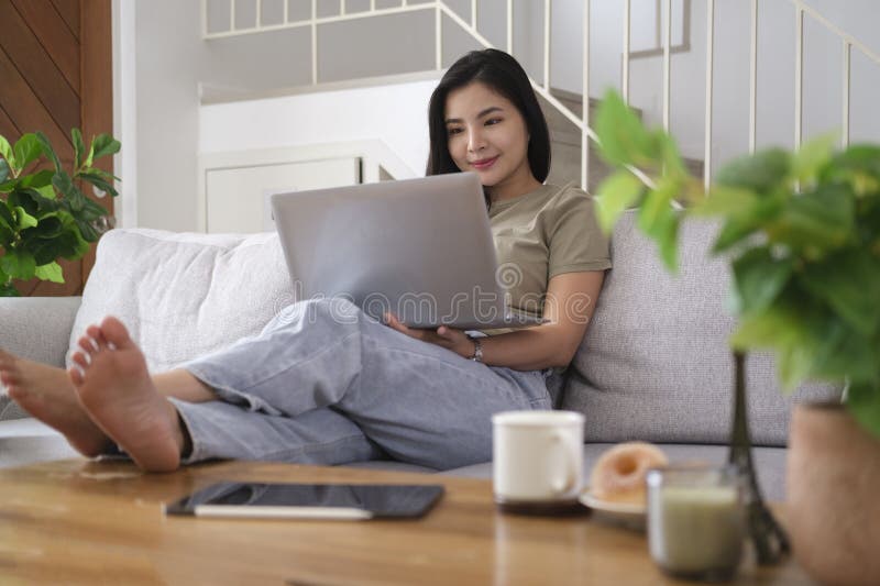 Smiling Asian Woman Sitting on Couch Using Laptop Computer Stock Photo ...