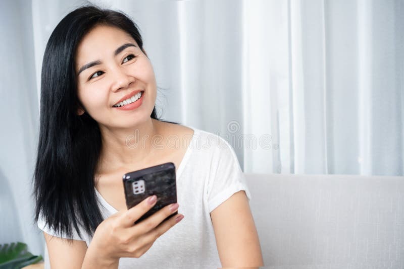 Smiling Asian Woman Using a Smartphone, Thinking and Daydreaming of ...