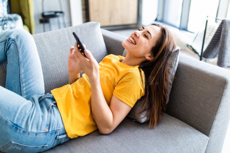 Smiling Beautiful Girl Using Mobile Phone Relaxing On A Couch At Home
