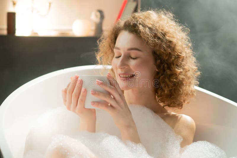 Smiling Beautiful Woman Lies In A Bath With Foam And Holds A Cup With