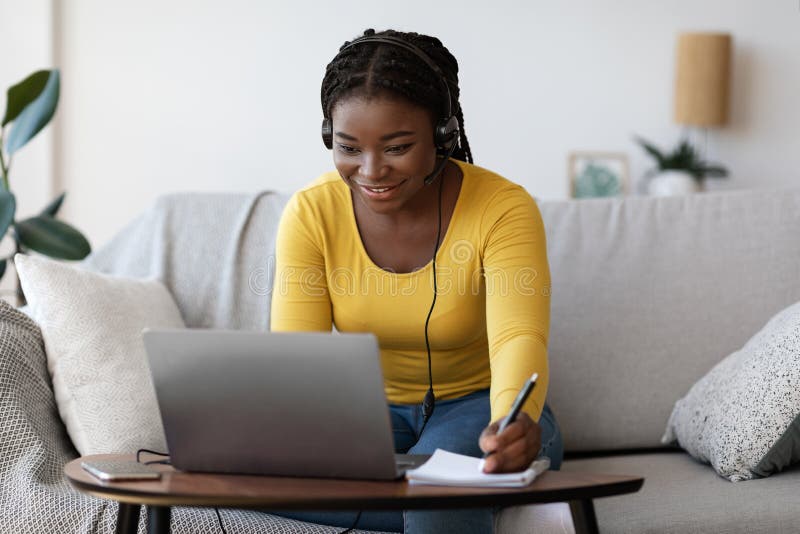 Smiling Black Lady In Headset Writing Notes While Watching Webinar On ...