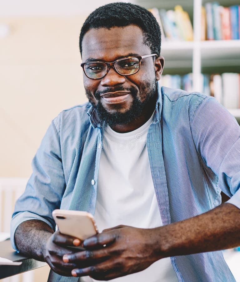 Smiling Black Man in Glasses with Cellphone Sitting at Working Desk ...