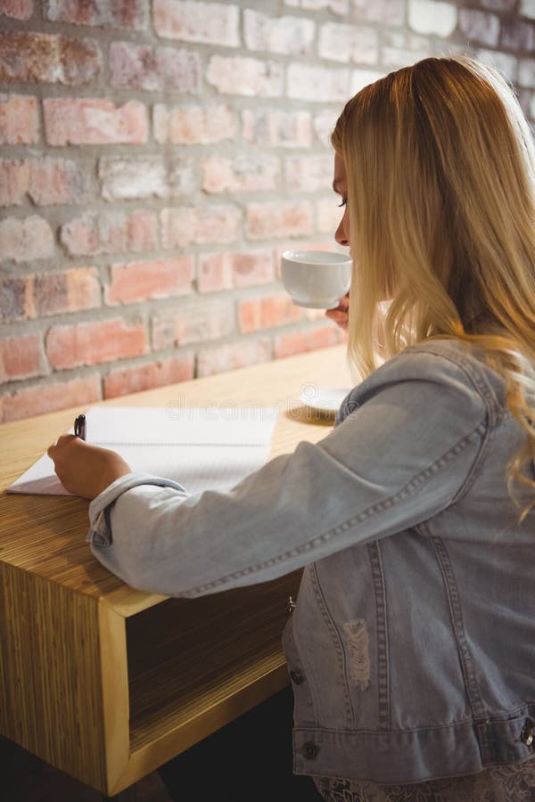 Smiling Blonde Drinking Coffee and Writing on Sheet of Paper Stock ...