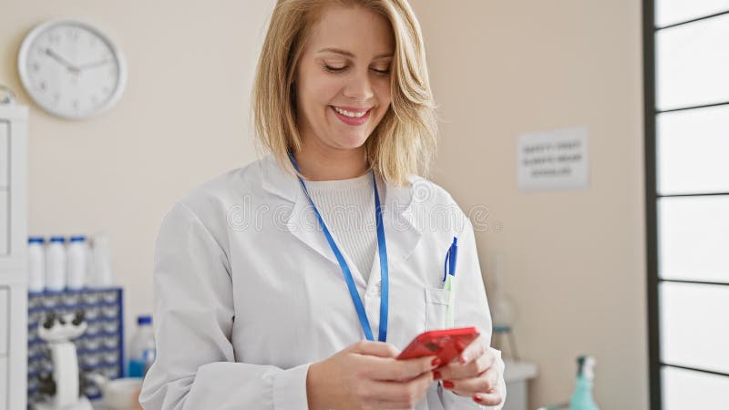 Smiling Blonde Woman in Lab Coat Using Smartphone in Clinic Stock Photo ...